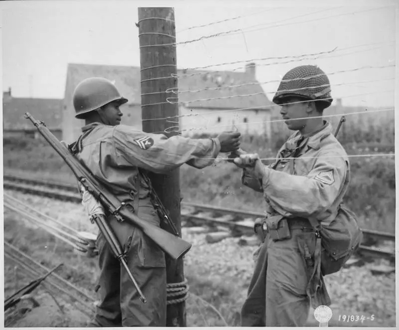 American Soldiers Repair Fence, Frankrike, 25. juli 1944 Begge jagerne er bevæpnet med karbiner M1 karbin. Soldaten i forgrunnen bærer også Springfield M1903-riflet. Photo Nara.