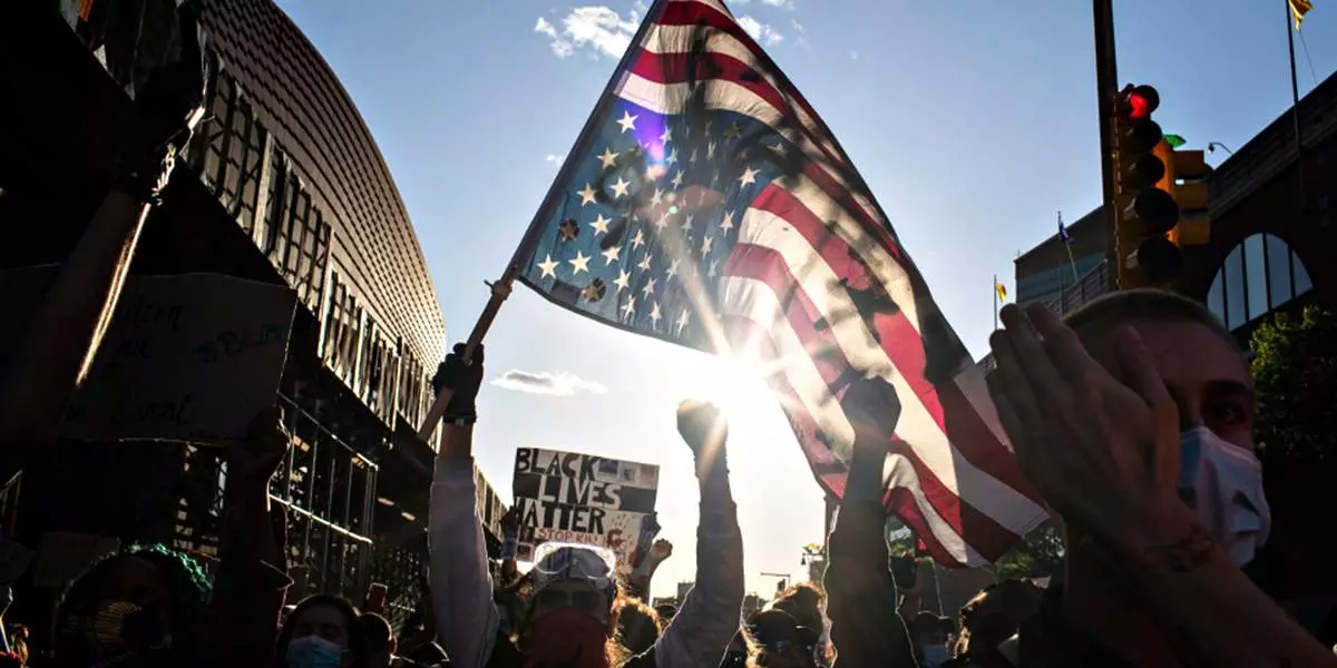 一个男人抱着美国。旗帜颠倒，遇险的迹象，作为抗议者在北乔治·弗洛伊德，2020年5月31日，在纽约布鲁克林自治市中心的团结集会期间。在整个城市中举行抗议活动，在弗洛伊德的死亡中，在明尼阿波利斯的警察习俗的黑人身上，在阵亡将士纪念日被警察受到限制后死亡。 （AP照片/ WONG MYE-E）